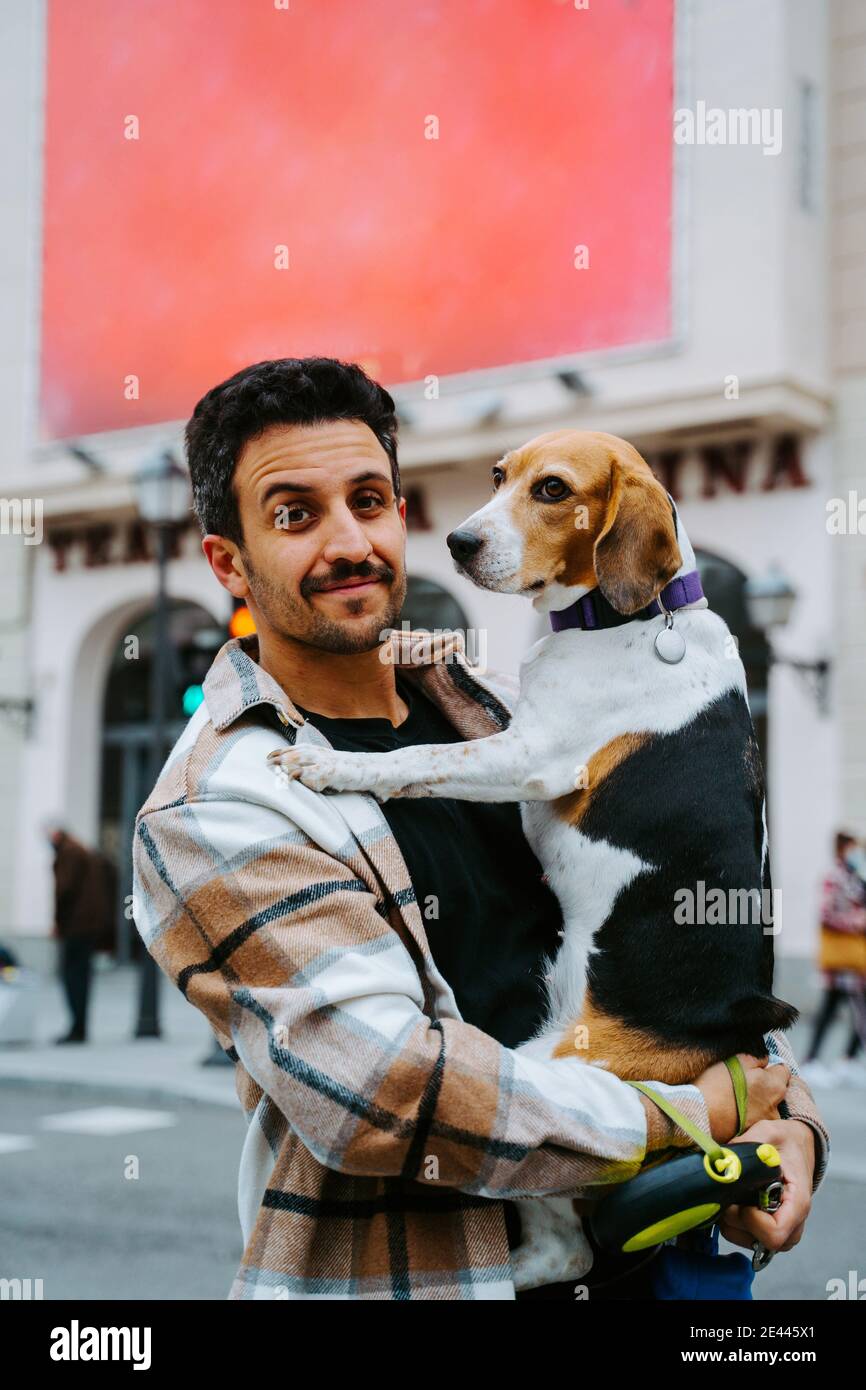 Content ethnic male owner with cute beagle dog standing on street and ...