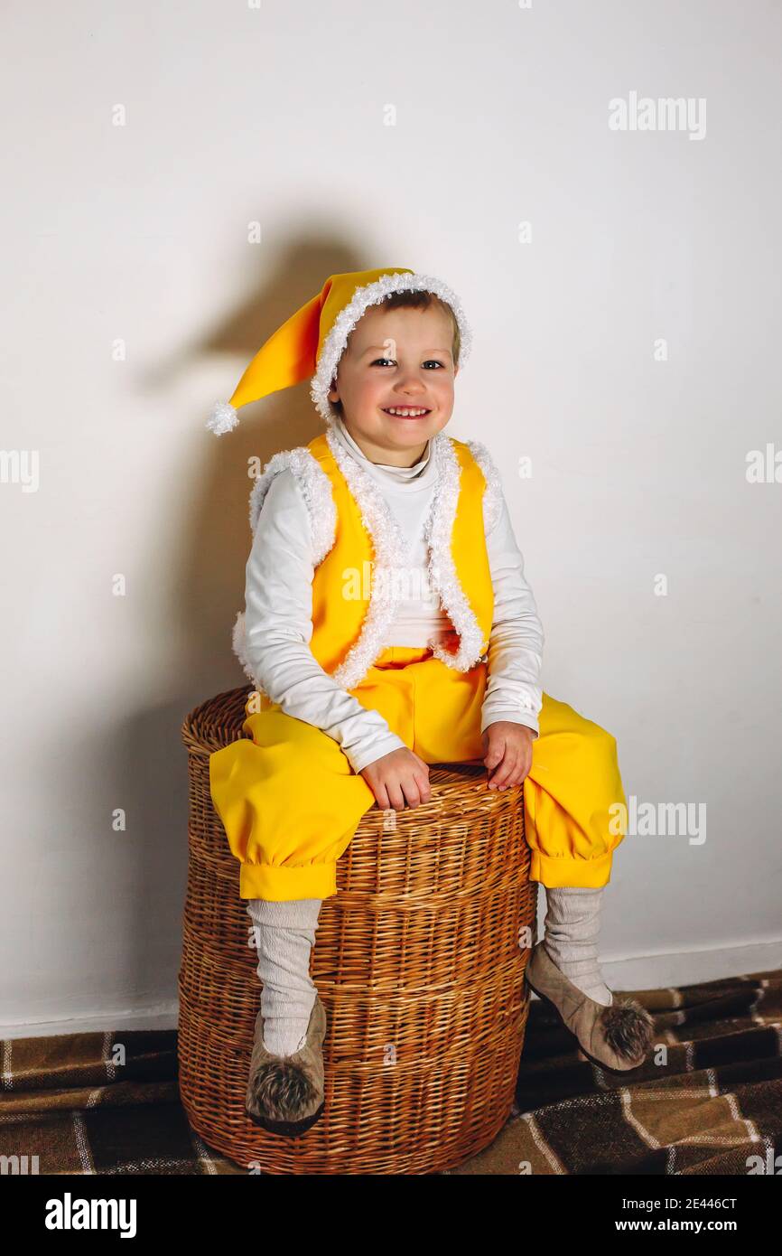 Little smiling boy sit on straw basket in yellow elf gnome outfit ...