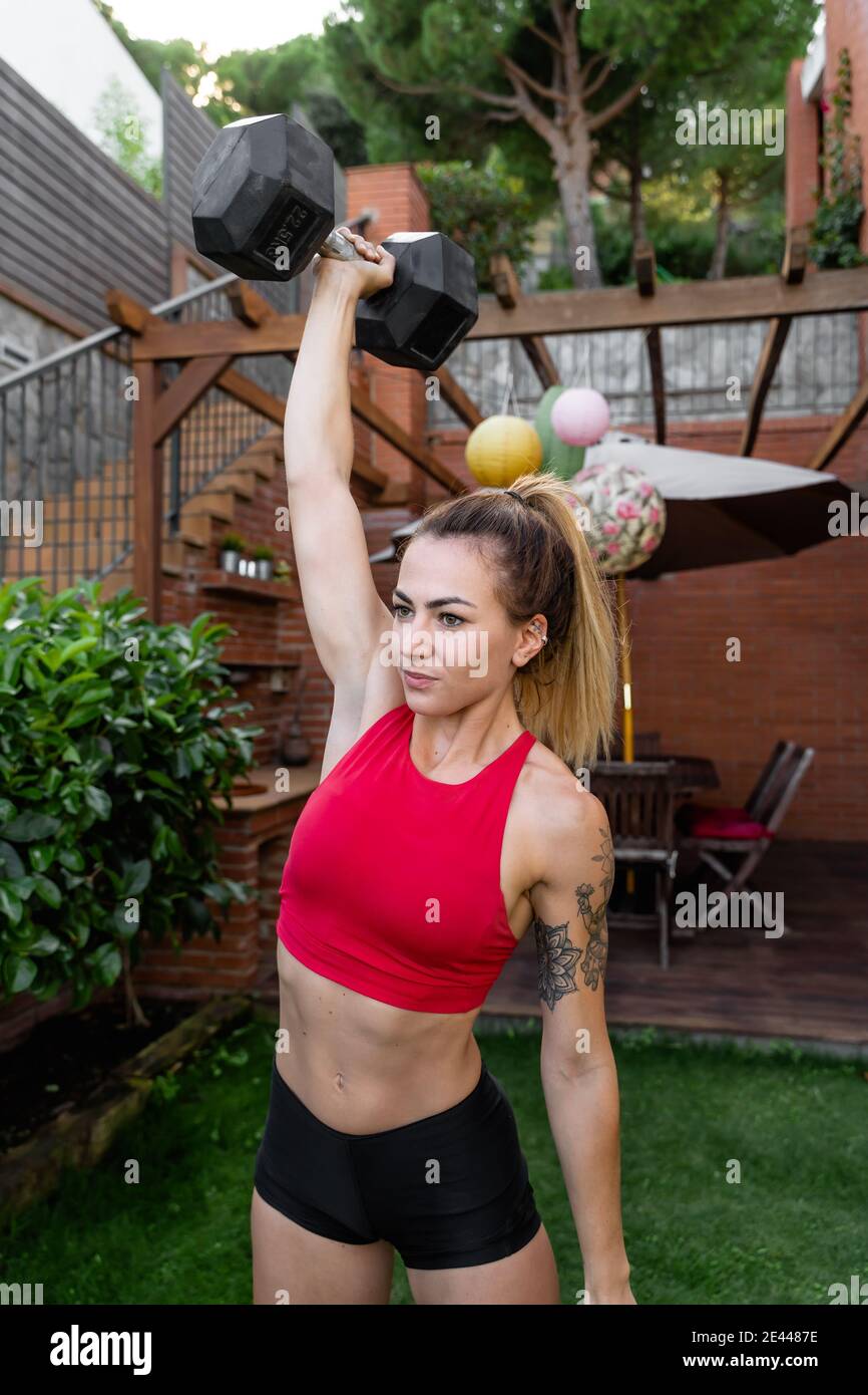 Cheerful athletic female lifting dumbbell during intense workout in ...