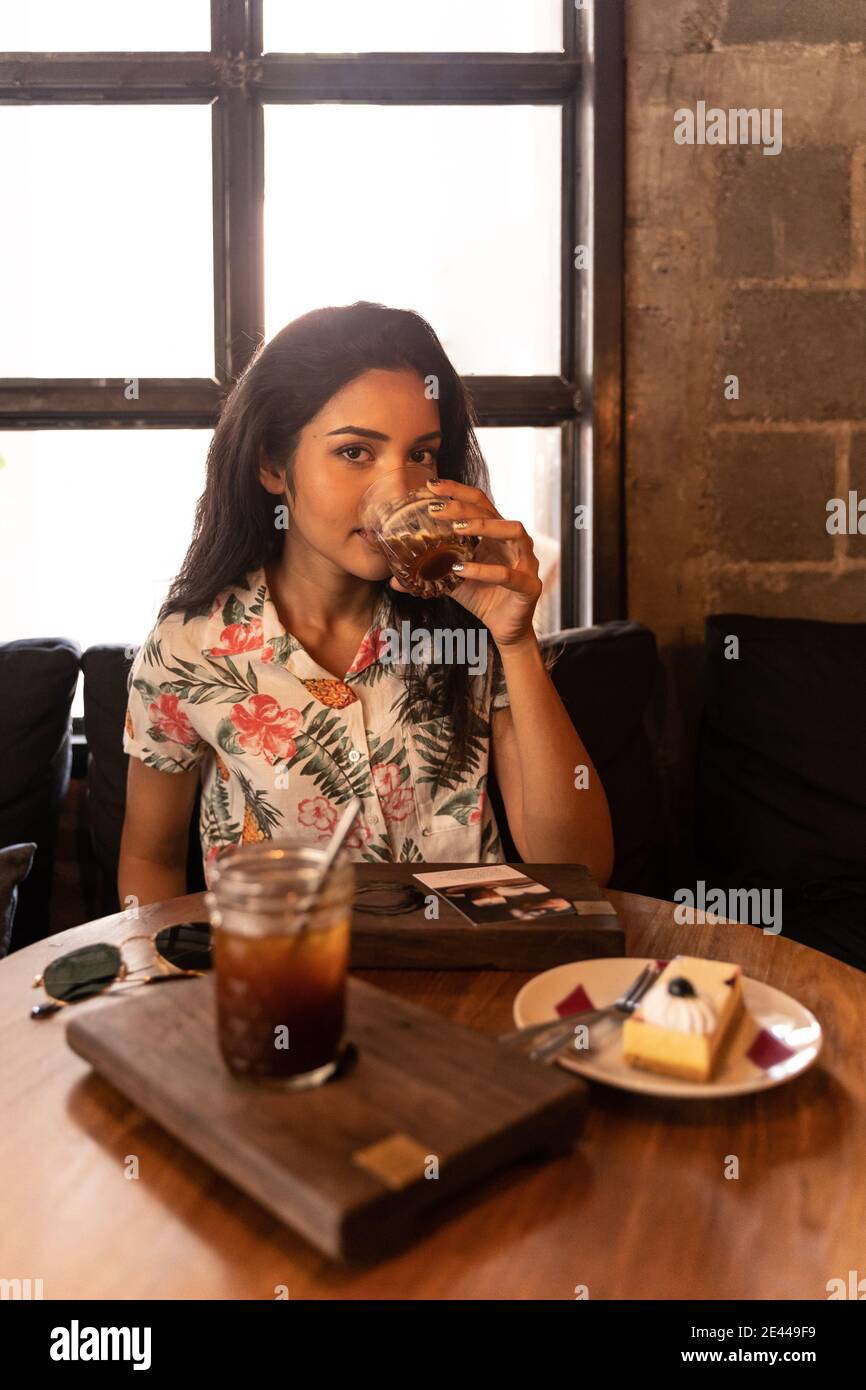Happy young ethnic indian female sitting at table with sweet dessert ...