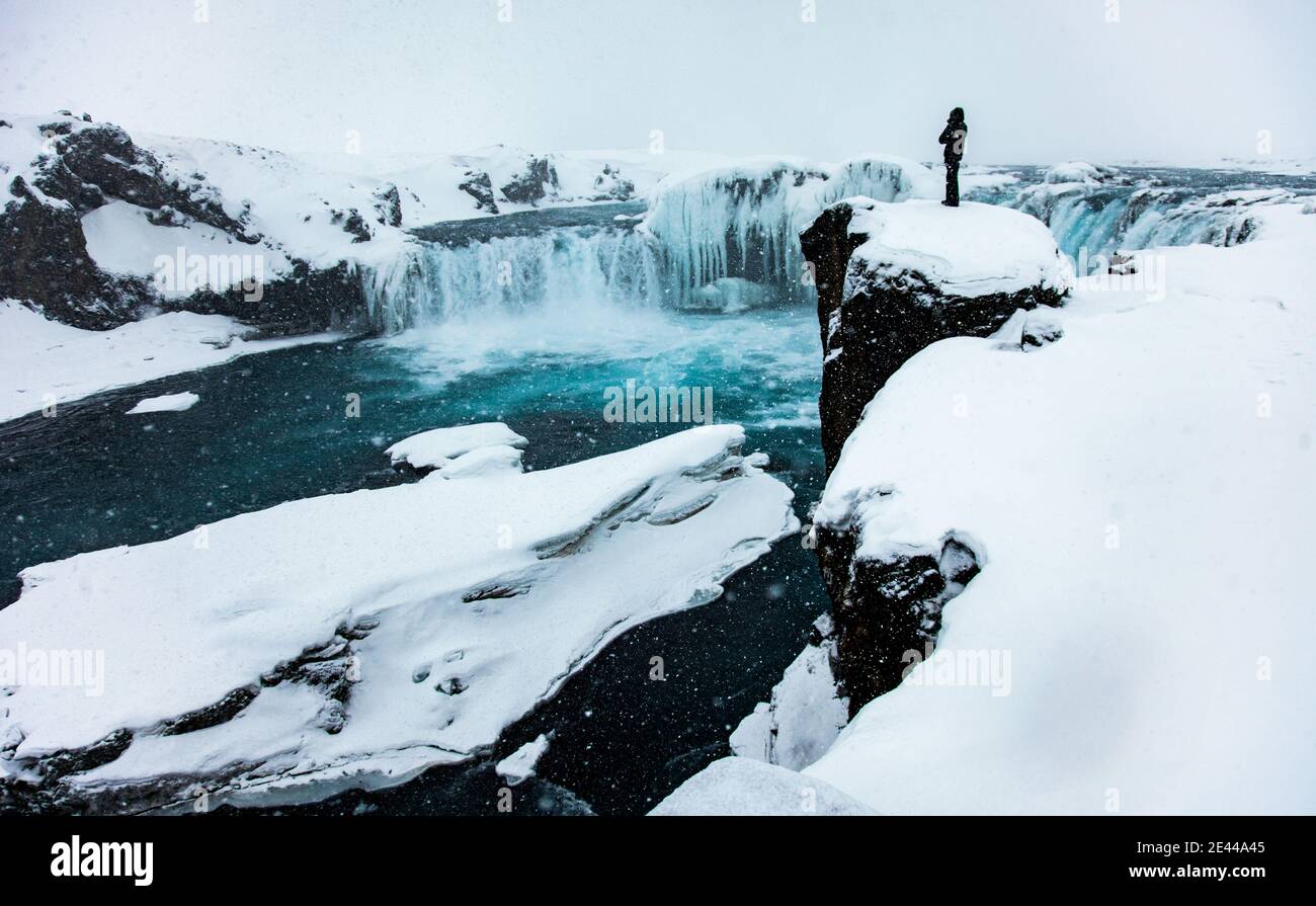 Distant view of explorer standing on edge of cliff and admiring scenery ...