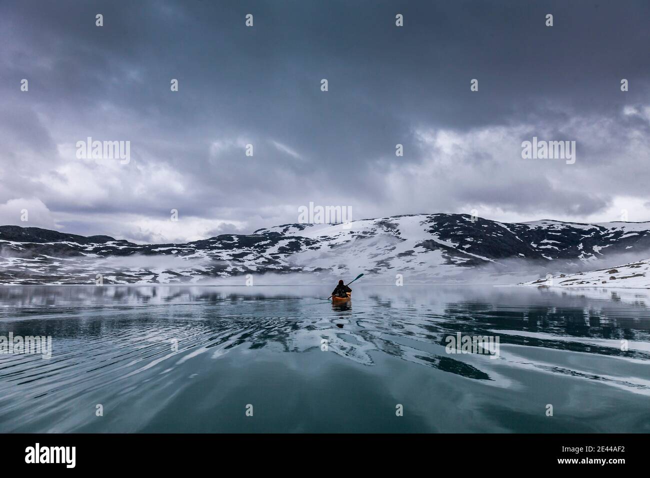 Back view of anonymous person floating in canoe along river in winter ...