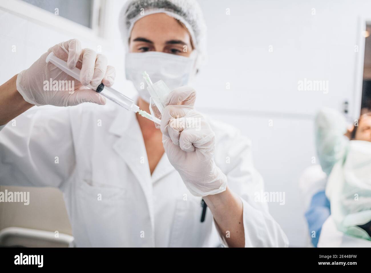 Doctor with mask, gloves and white cap covering a needle filled with ...
