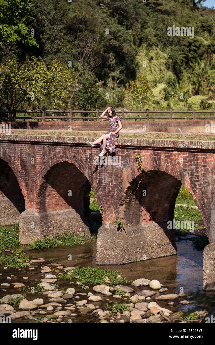 Side view of Asian female in dress sitting on old Daping Red Bridge and ...