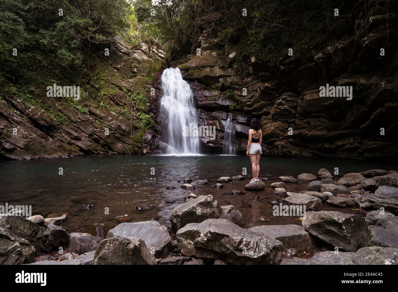 Side view of female tourist standing on rock near Tiemu Falls in forest ...