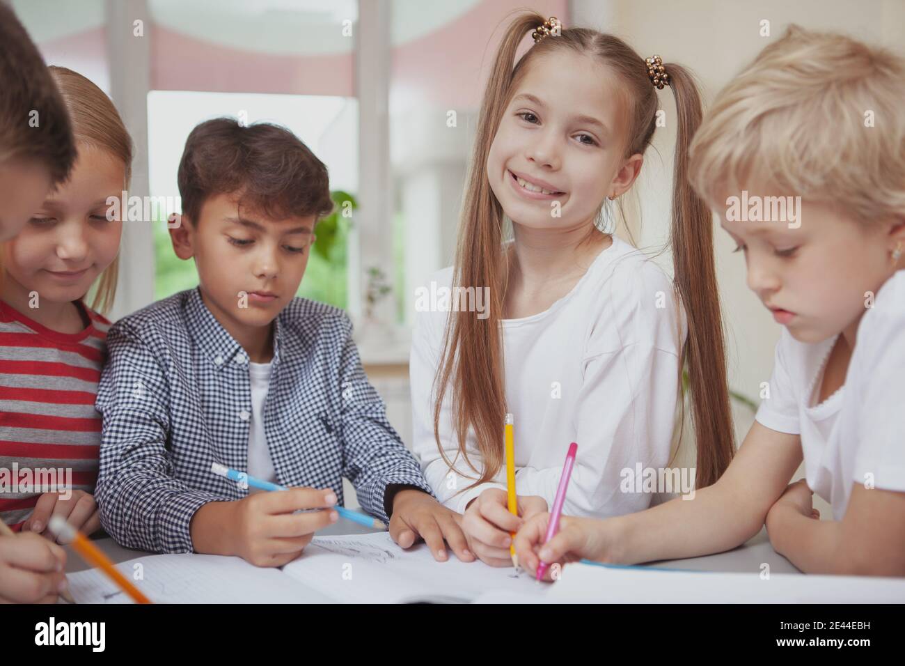 Cheerful beautiful little girl smiling to the camera while drawing at ...
