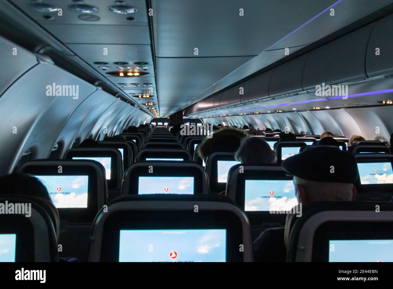 Plane cabin by night lit from the seat screens with people on board ...
