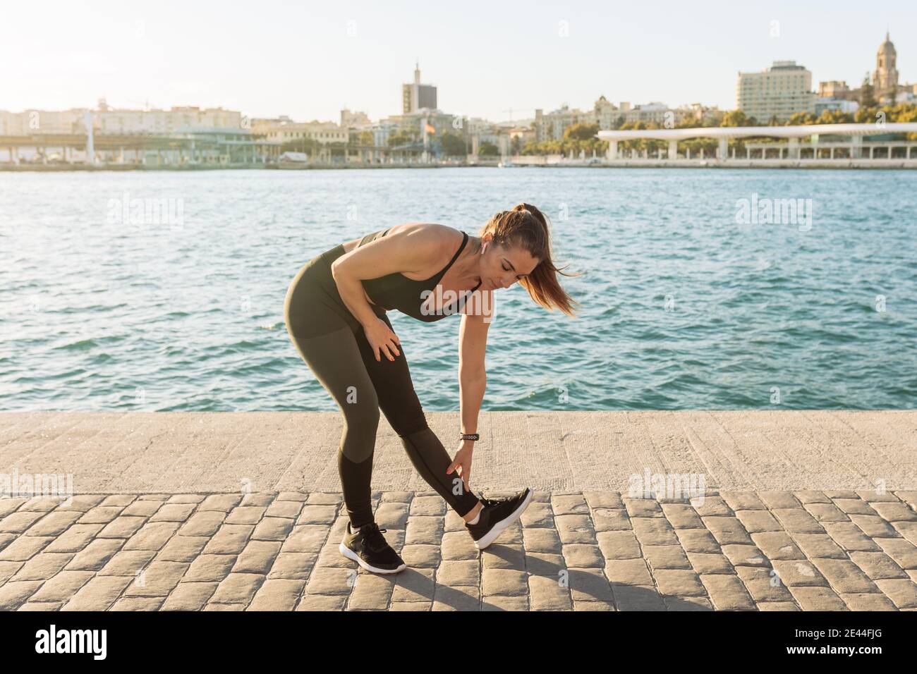 Full body side view of fit female in black sportswear stretching legs ...