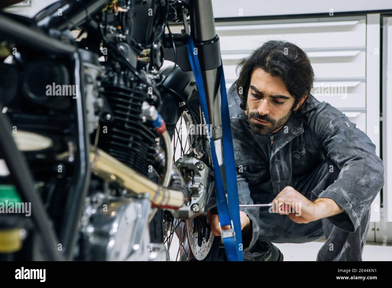 Busy male technician in uniform repairing wheel of shiny motorbike with ...