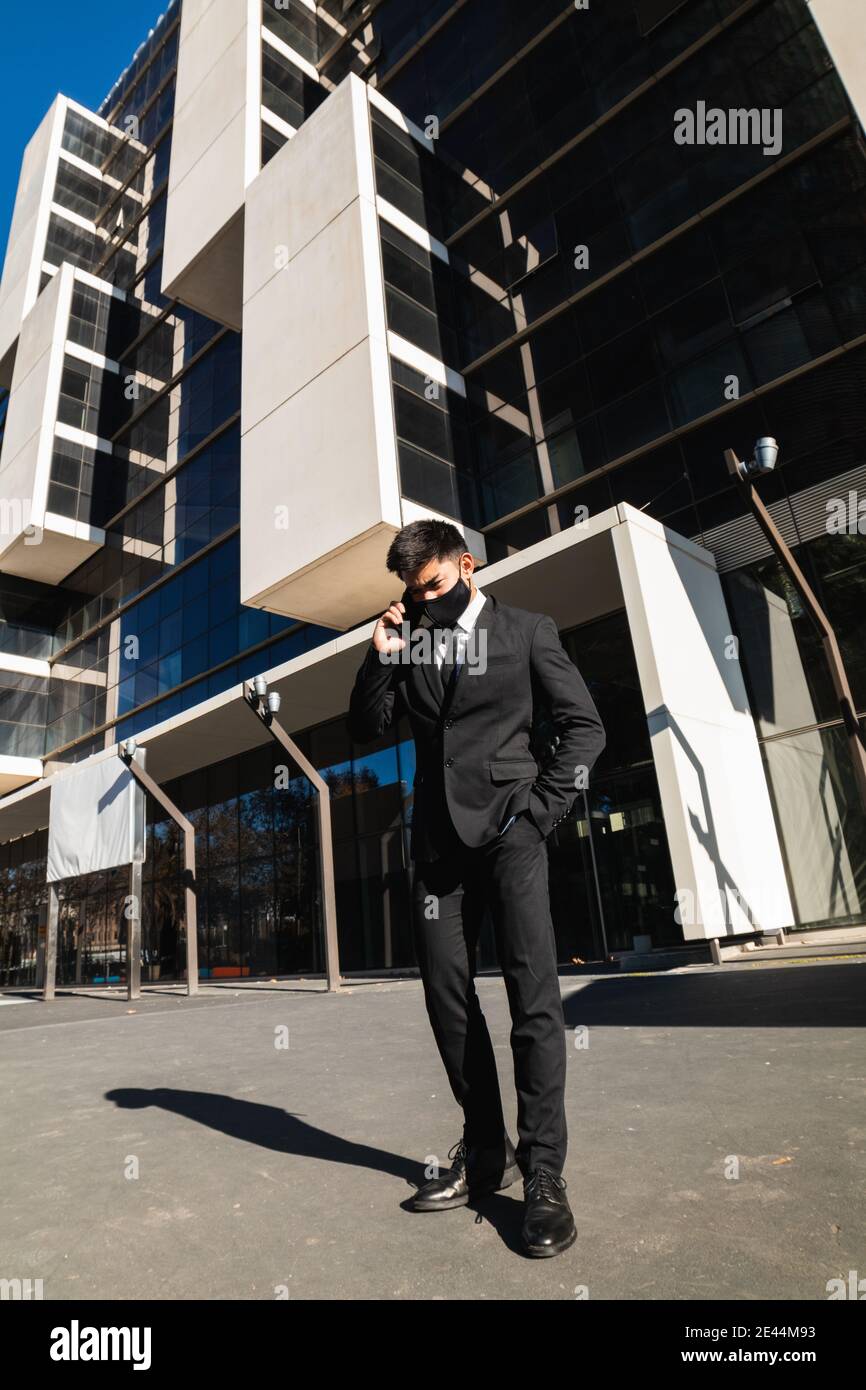 Low angle of male entrepreneur in formal suit and protective mask ...