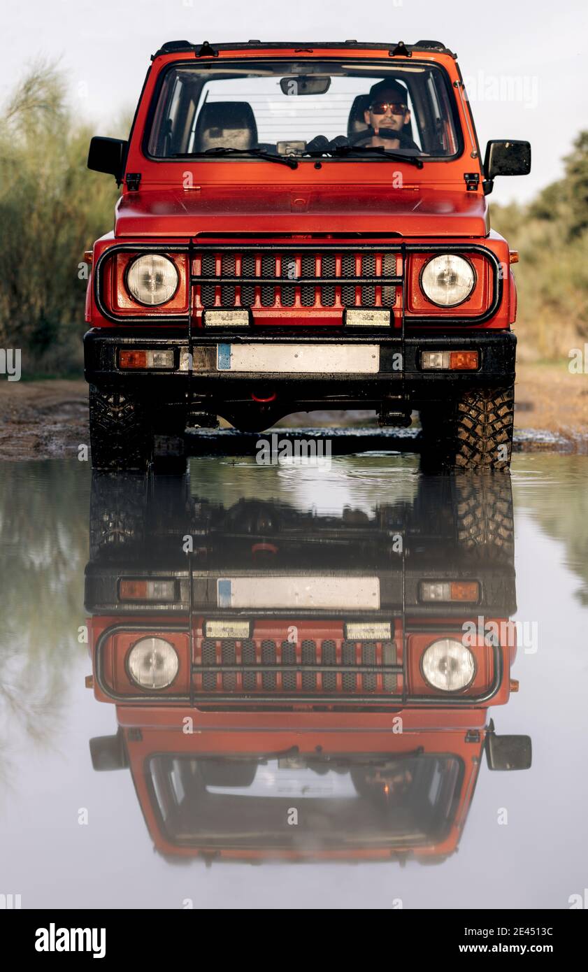 Modern red off road vehicle with male driver reflecting in surface of ...