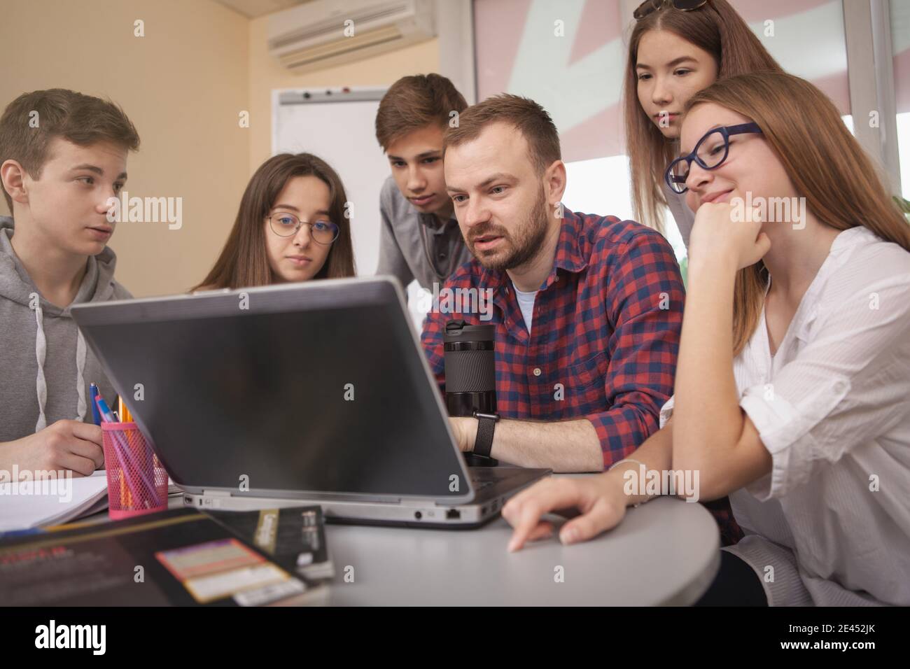 Helpful male teacher using laptop at class, working on a project with ...