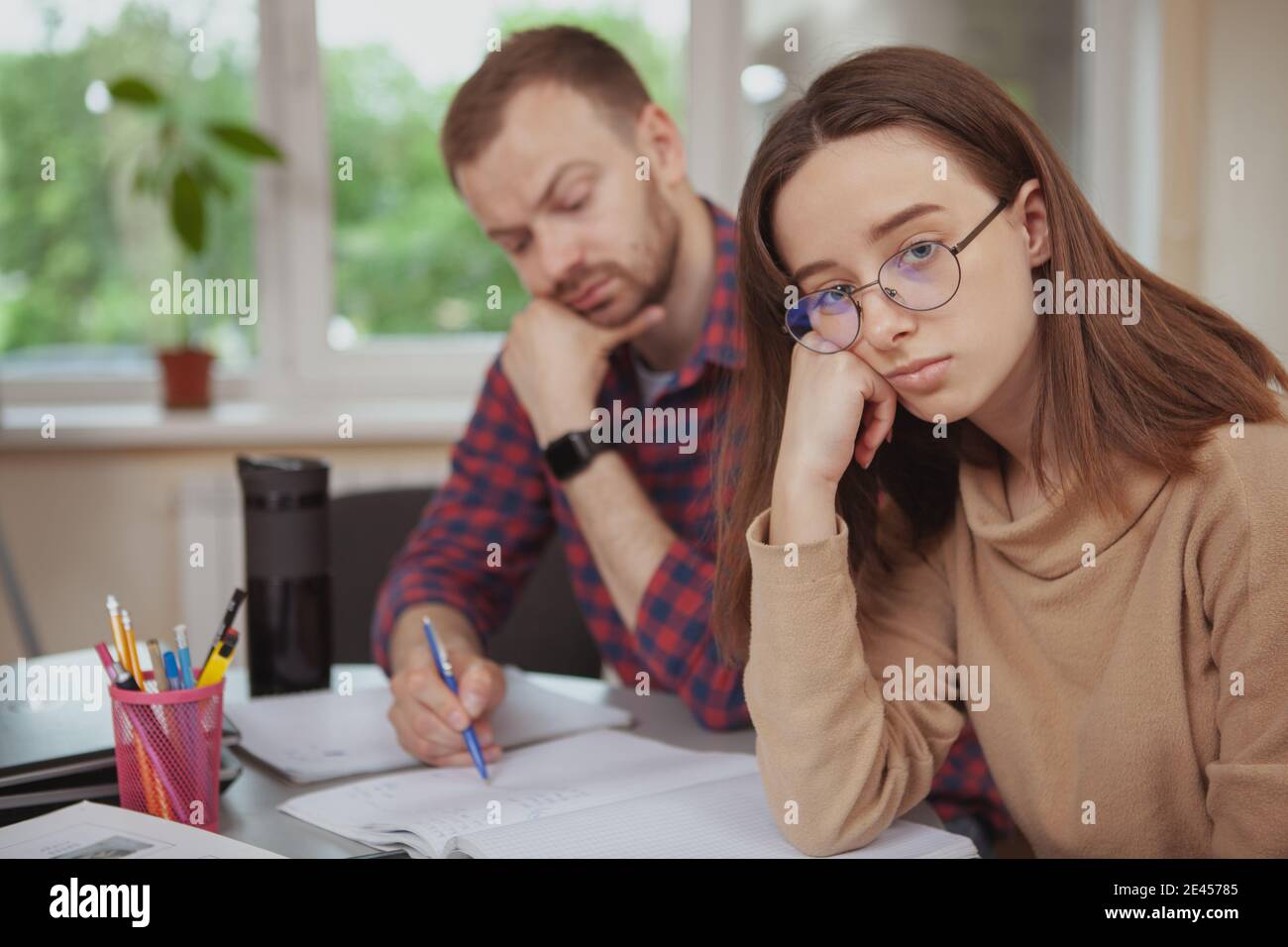 Teenage girl looking bored while studying with a tutor in class, copy ...