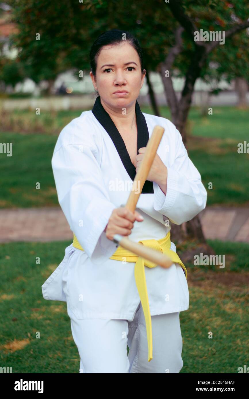 Vertical shot of a female in dobok practicing taekwondo with nunchakus ...