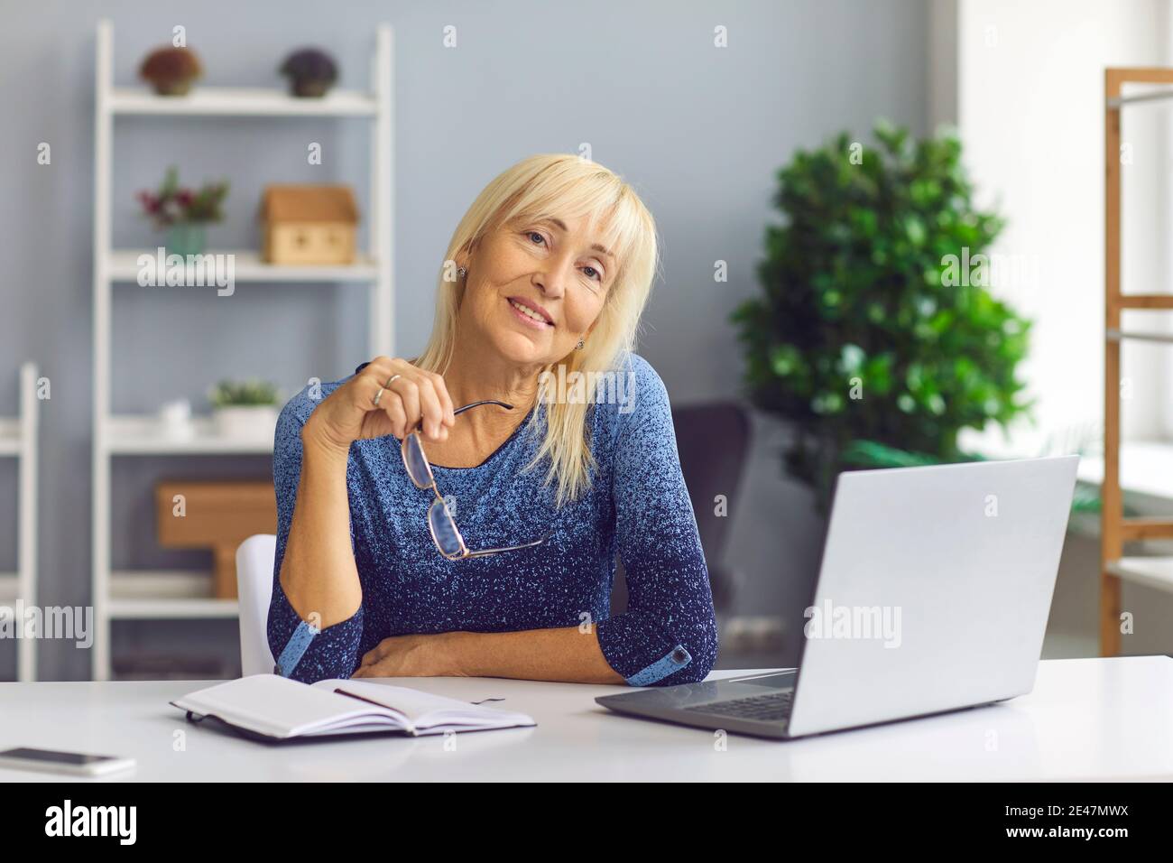 Positive middle aged woman worker sitting in office looking at camera ...