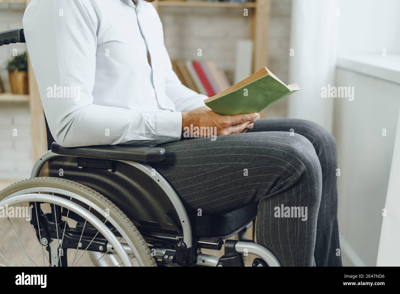 Disabled man in wheelchair reading a book indoors Stock Photo - Alamy