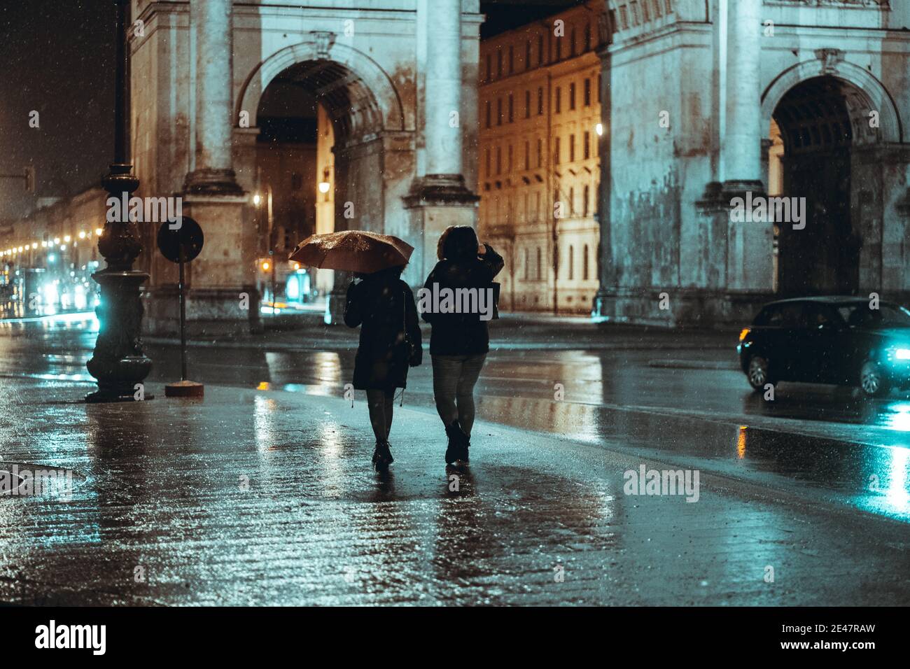 Back view of two female friends walking on the sidewalk under the rain ...