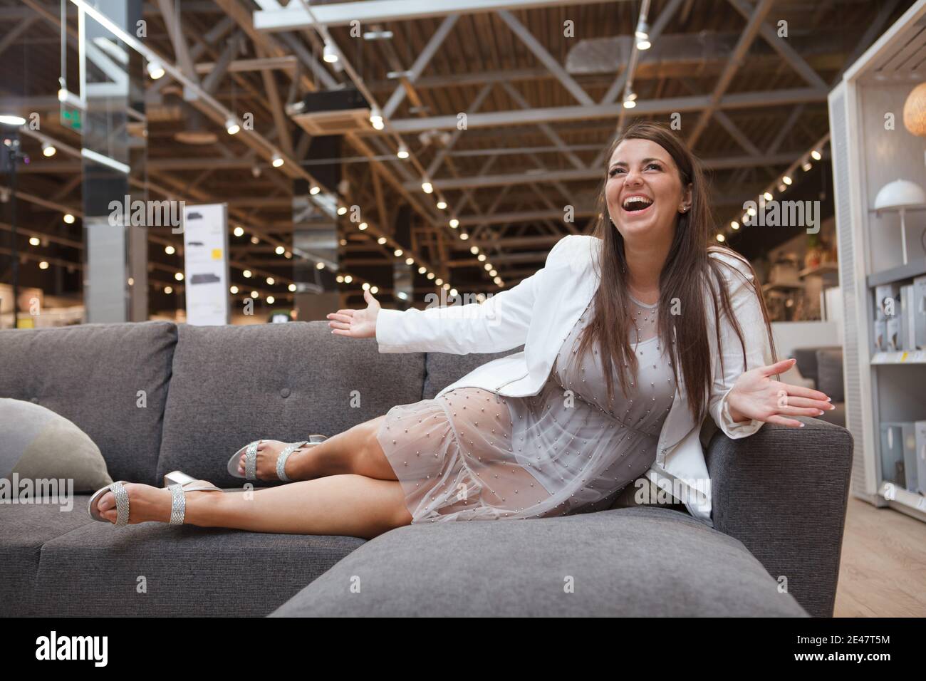 Excited curvy woman laughing, sitting on a new couch at furniture store ...