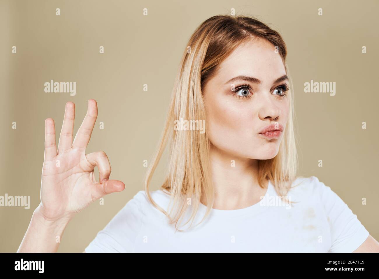 Cheerful blonde woman in a white T-shirt gestures with her hand emotions beige background Stock ...
