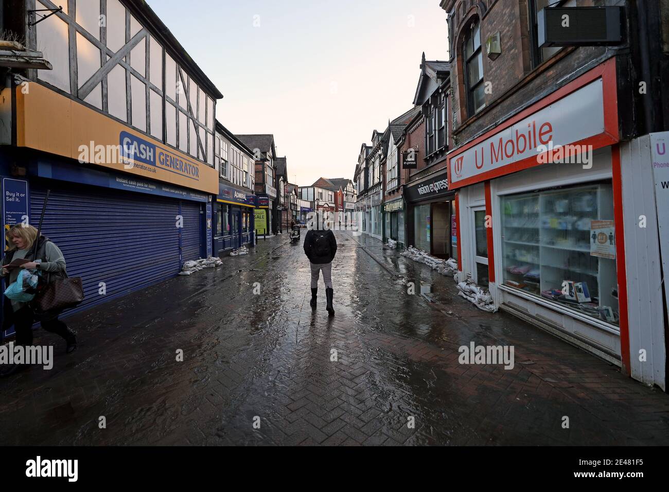 A man walks through the remaining flood water outside the shops in the ...