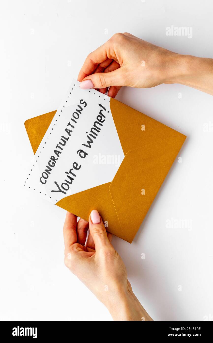 Hands holding award congratulation card in golden envelope. Text You're ...