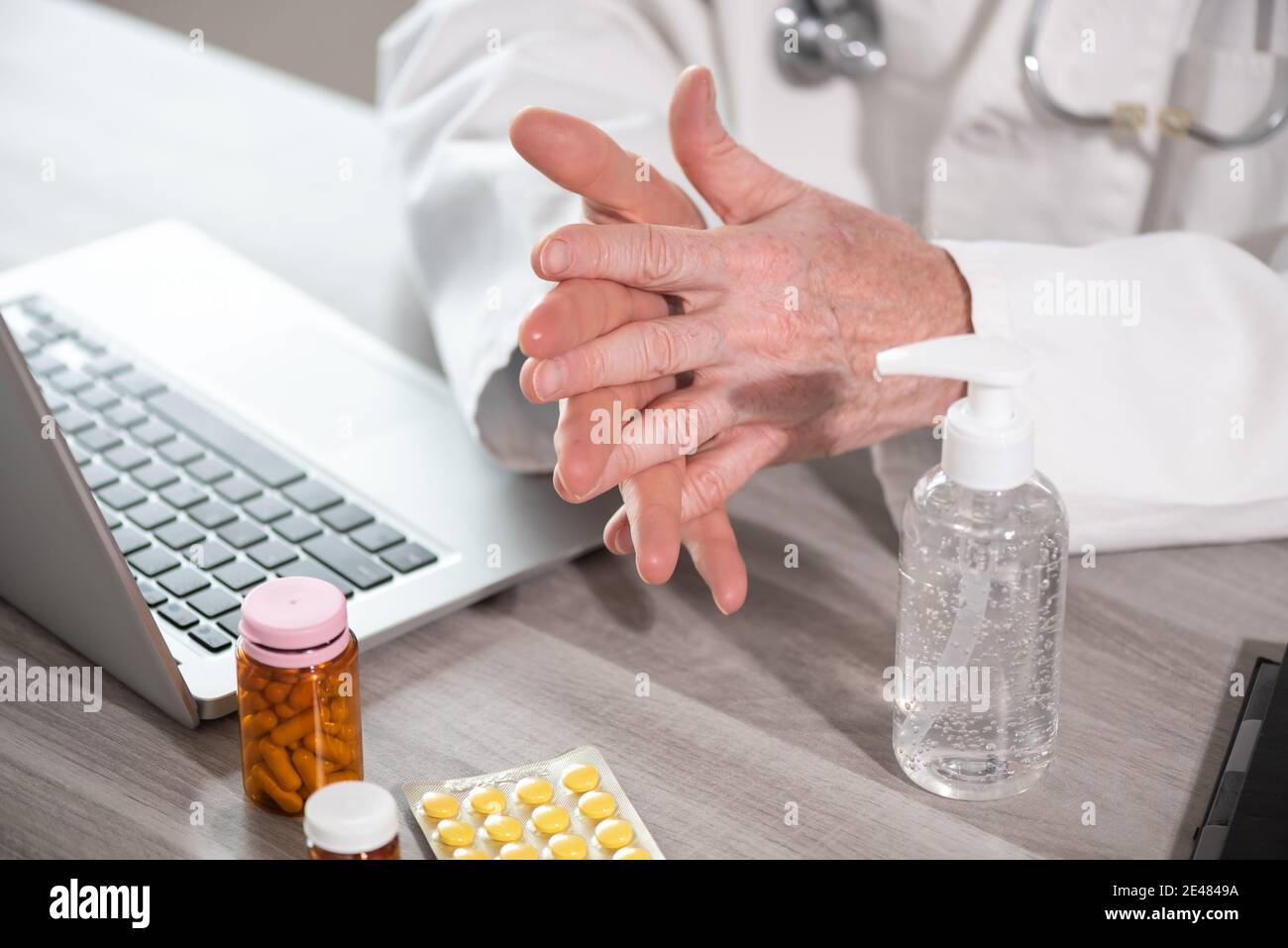 Doctor rubbing his hands with sanitizer alcohol gel in medical office ...