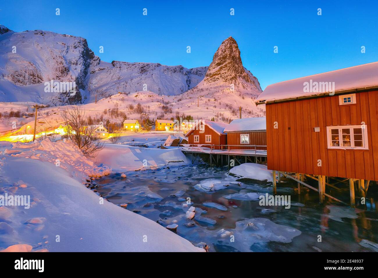 Dramatic evening cityscape of Reine town. Red rorbuers on the shore of ...