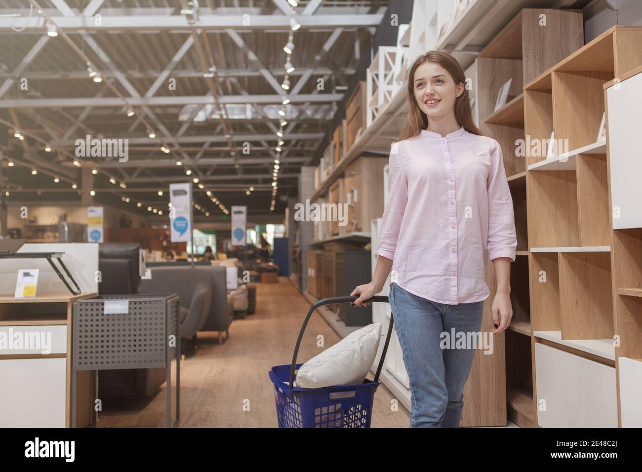 Attractive female customer walking with shopping cart at furniture ...