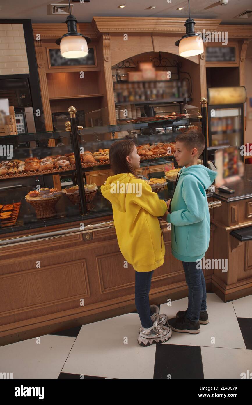 Vertical full length shot of two kids talking, choosing pastry at local ...