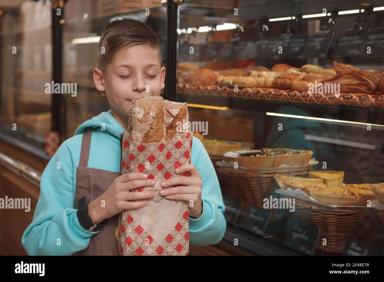Lovely young boy wearing apron, smelling fresh bread at his family ...