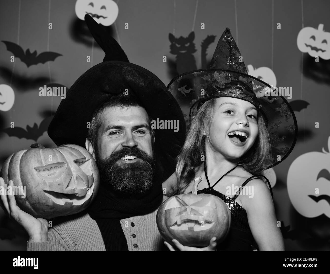 Wizard and little witch in black hats hold pumpkins. Girl and bearded ...