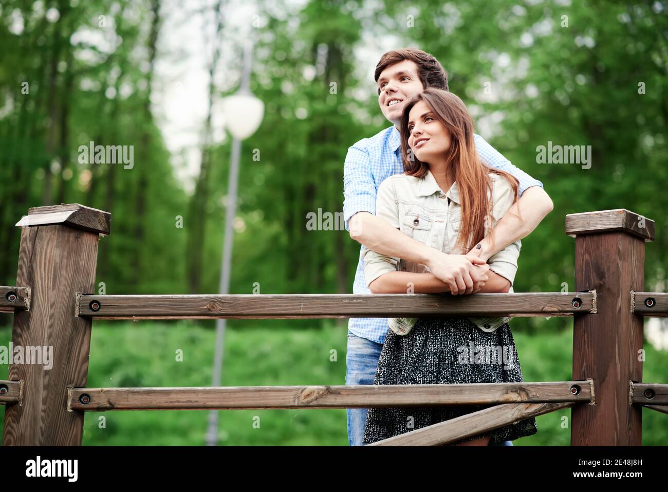 Young man hugging his girlfriend in the summer park near the railing ...