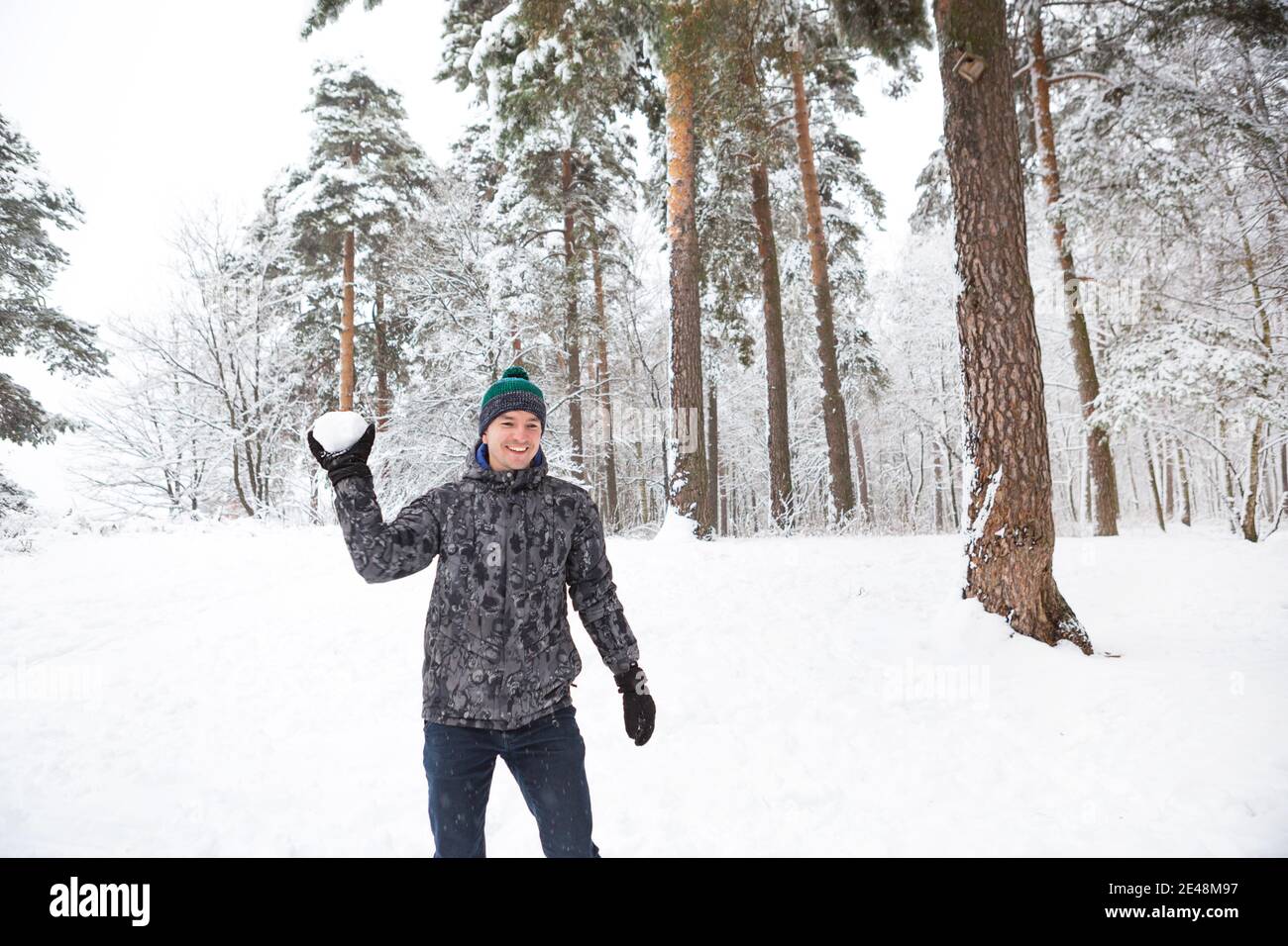 A young man with a snowball in his hand is having fun, swinging for a ...