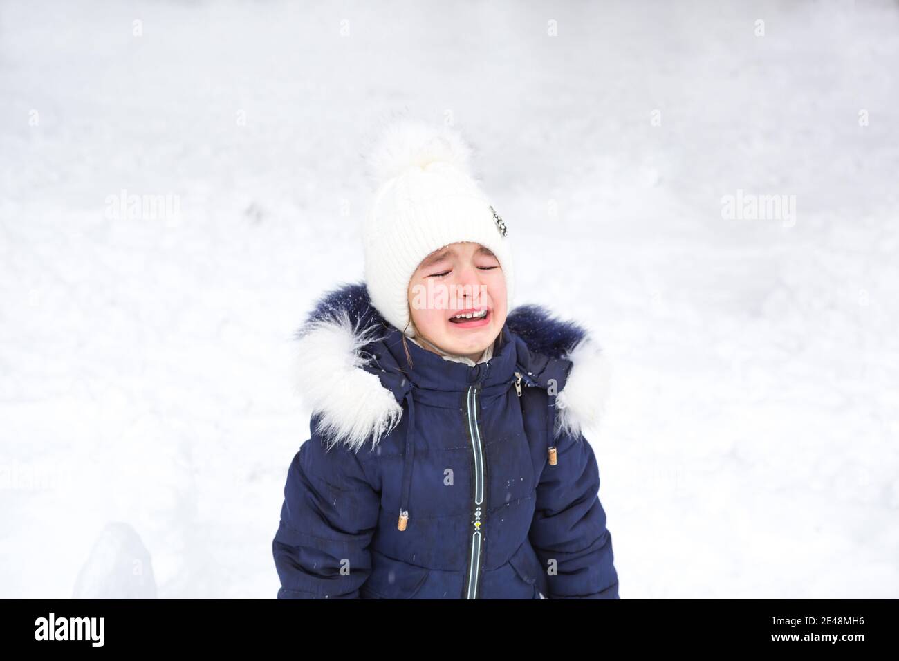 Little girl crying outside in winter. A child in warm clothes is upset ...