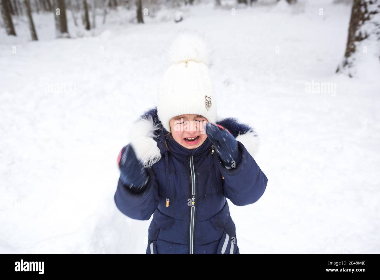 Little girl crying outside in winter. A child in warm clothes is upset ...