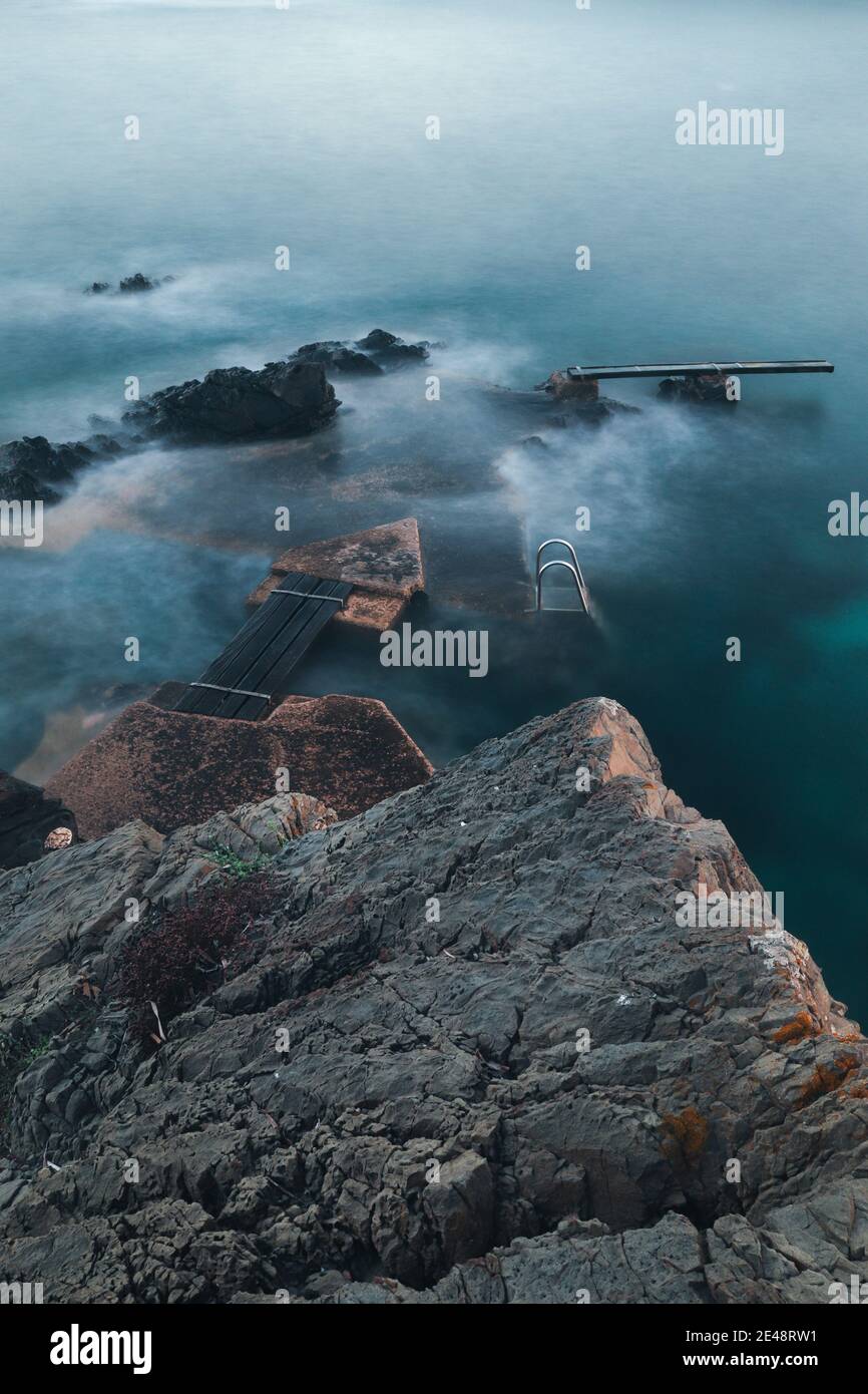 Aerial shot of the ocean with a swimming pool near the rock in Spain ...