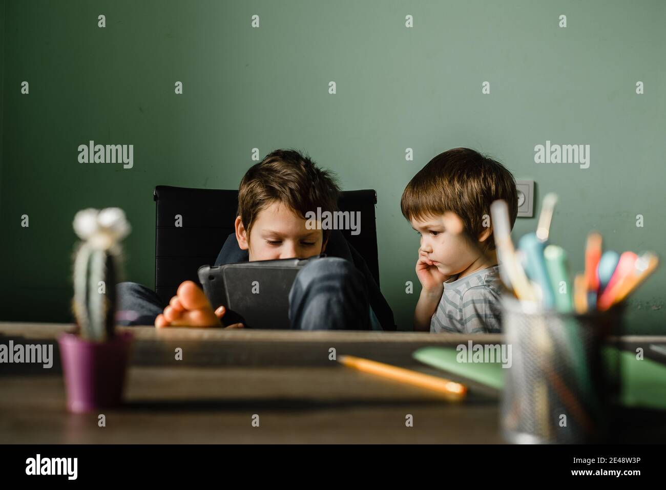 Junior boy with his brother playing tablet at home, growing up with ...