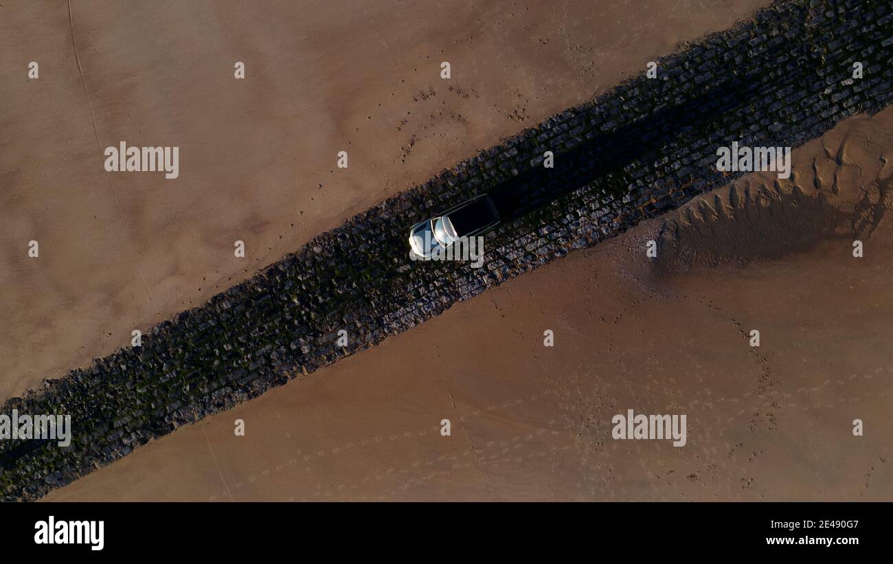 Aerial view of a car driving through a paved road amid the sandy shore ...
