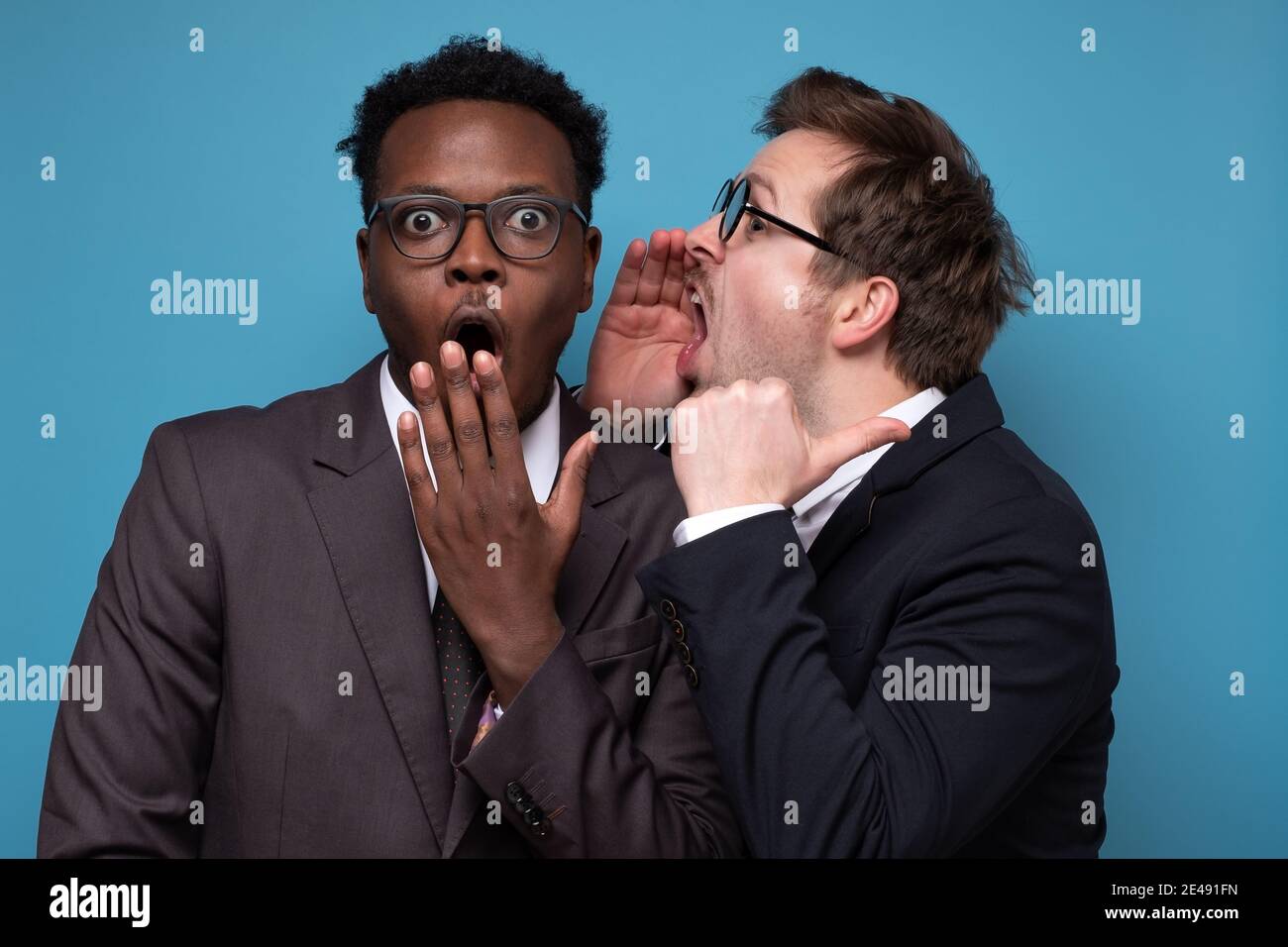 Caucasian man whispering to his african coworker ear telling him ...