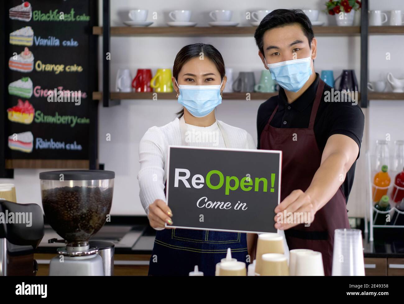 The shopkeeper and barista, wearing a face mask, holds an ReOpen! sign ...