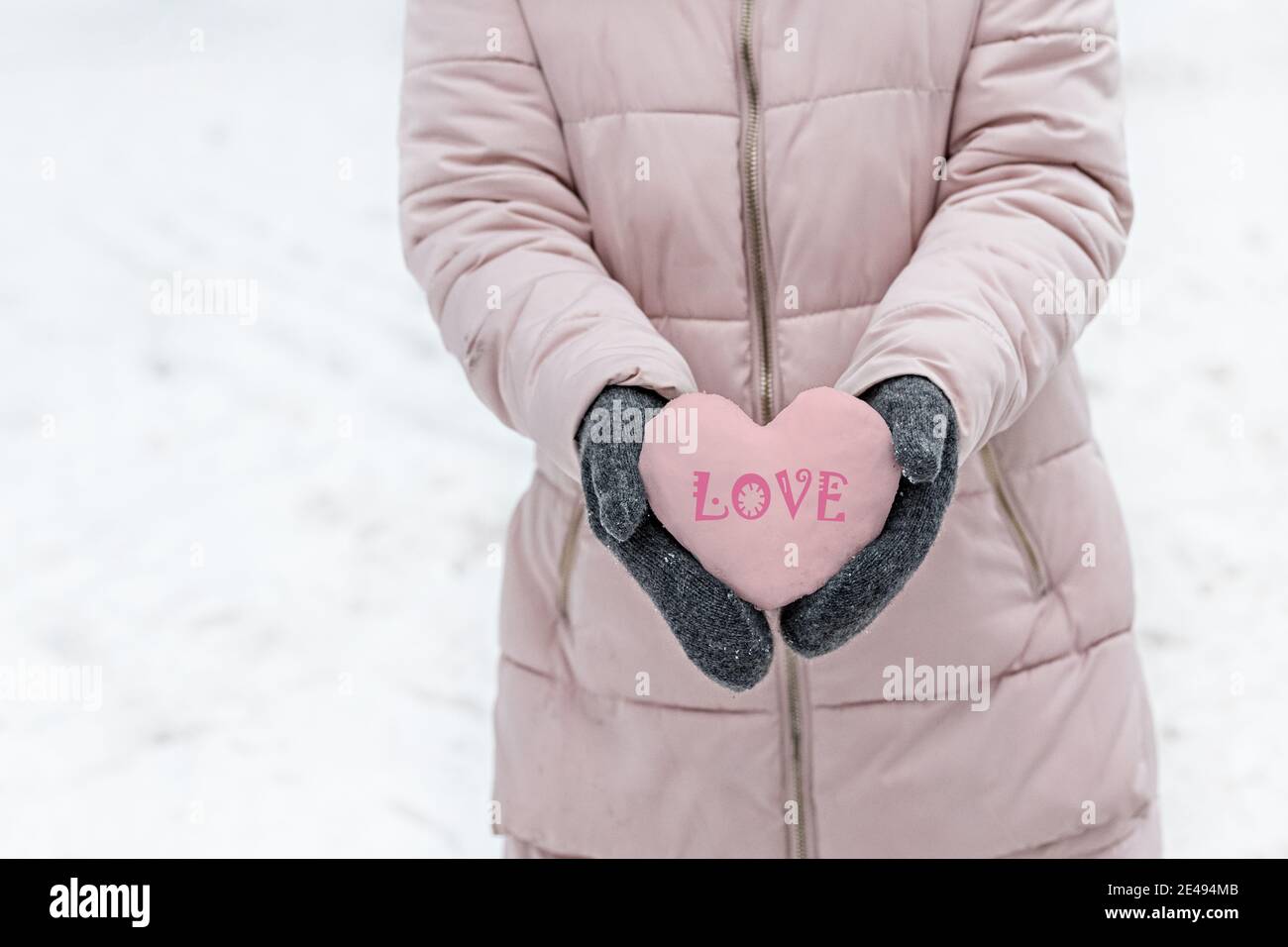 Women's hands in warm gray mittens with a snowy pink heart. The Concept ...