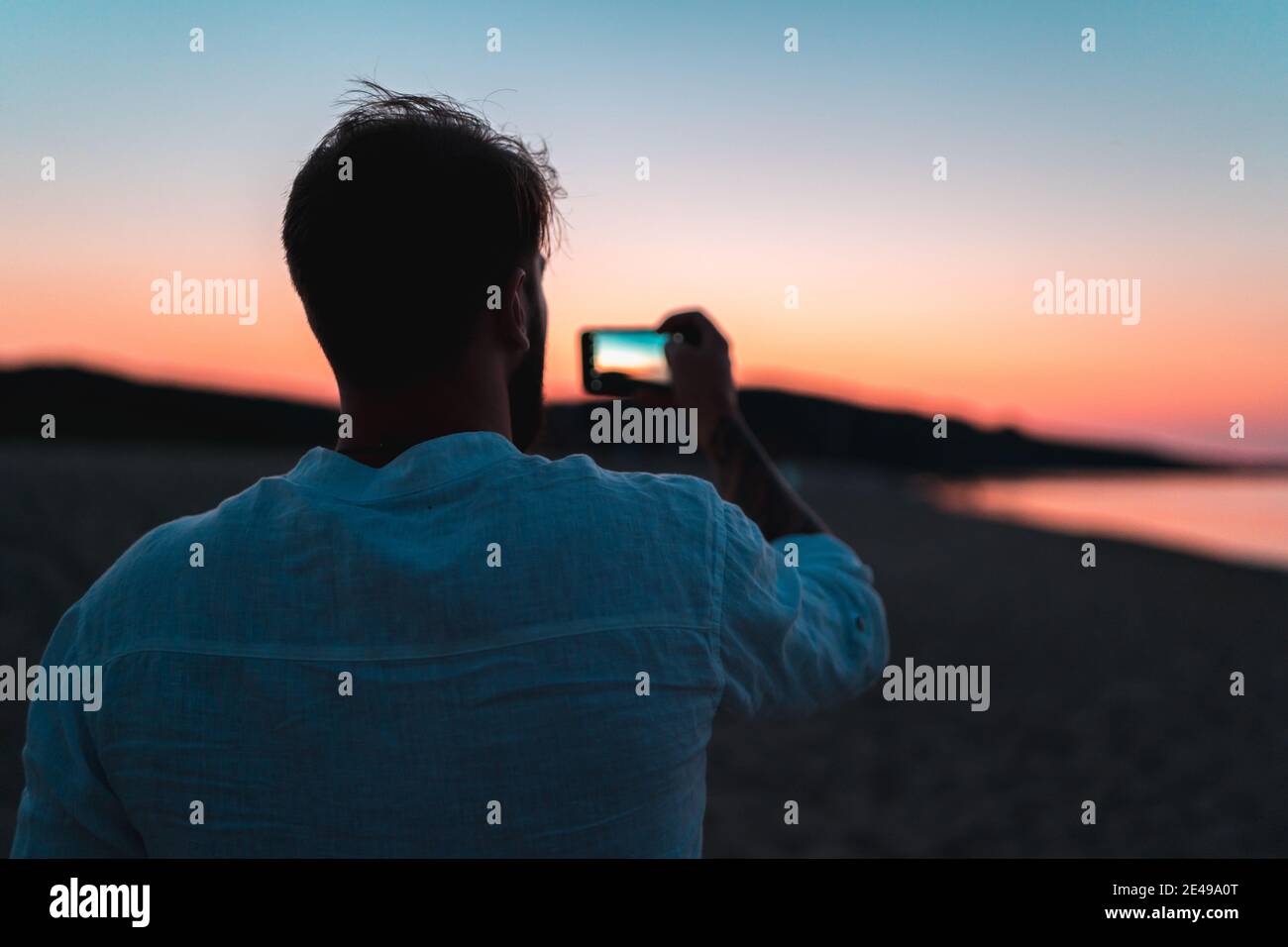 Back view of young man taking photo of colorful sunset over the sea ...