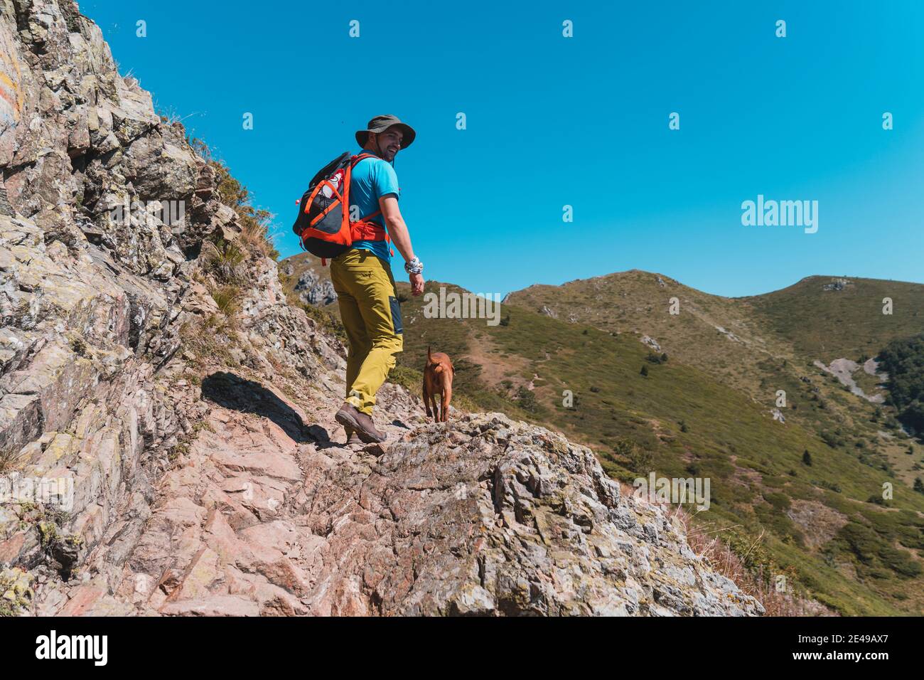 Happy young man hiker walking on rocky mountain ridge with his dog ...