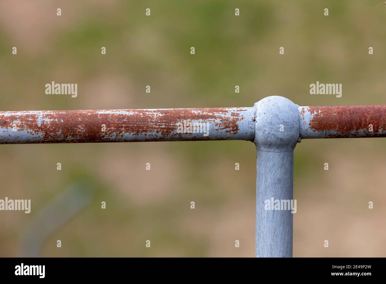 A rusty steel galvanised fence post and hand rail on a green grass ...