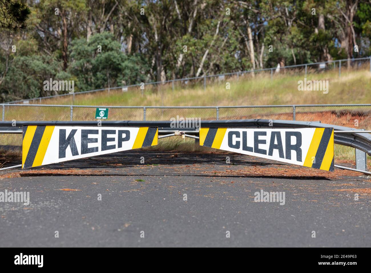 A safety keep clear boom gate on a road near bushland and a steel fence ...