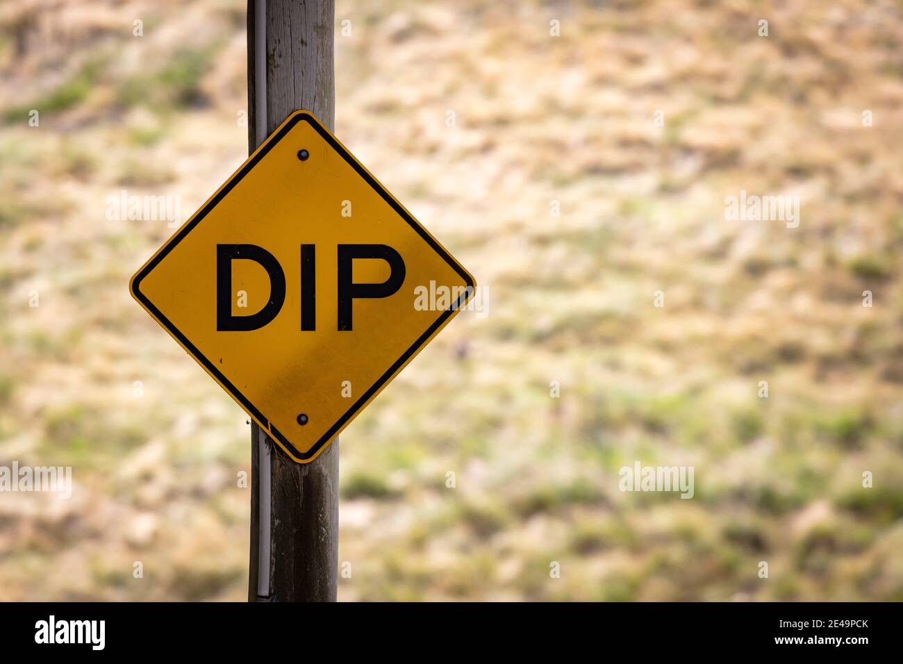 A yellow safety sign attached to an old wooden post signifying a dip in ...