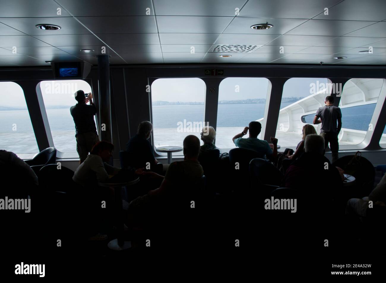 A group of tourists aboard a ferry look out the large windows. Ship ...