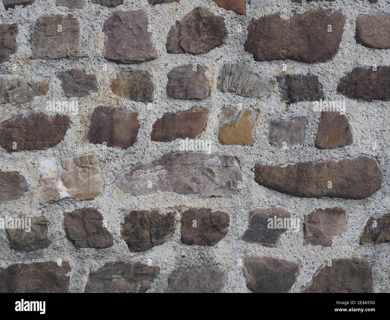 A wall with masonry of various shapes of stone and thick gray layer of ...
