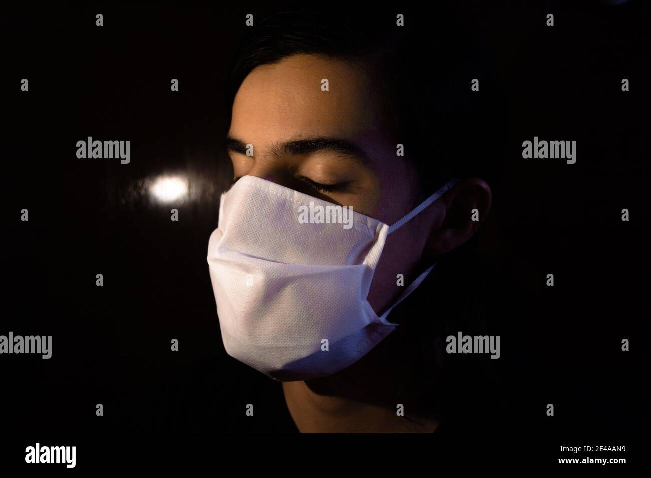 Portrait of a young man with a disposable white face mask, closed eyes ...