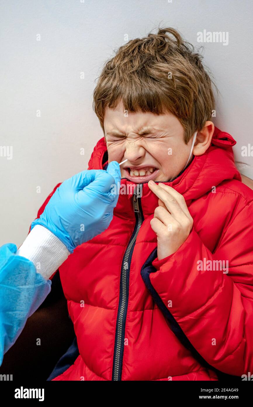 Doctor tacking a coronavirus test to an elementary age boy's nose with ...